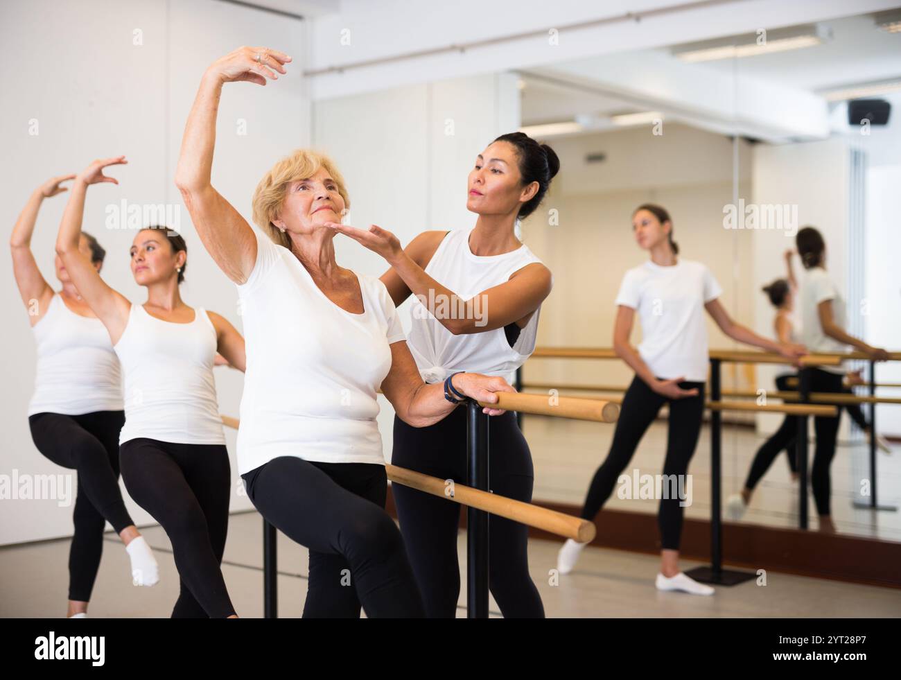 Female ballet trainer teaching group of dancers near ballet barre in ...