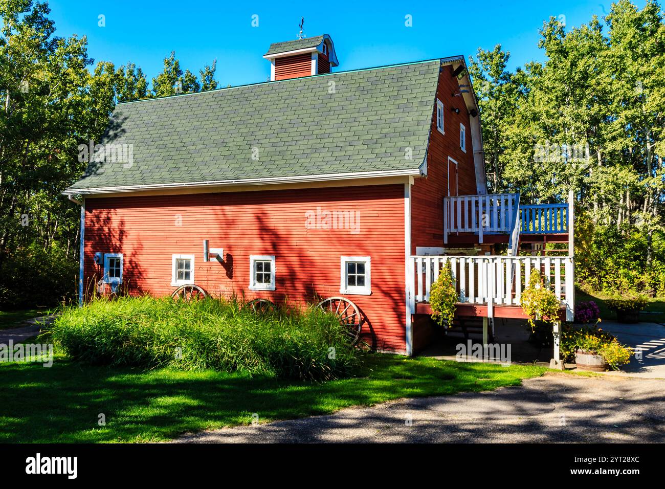 A red barn with a green roof and white trim. The barn has a porch with ...