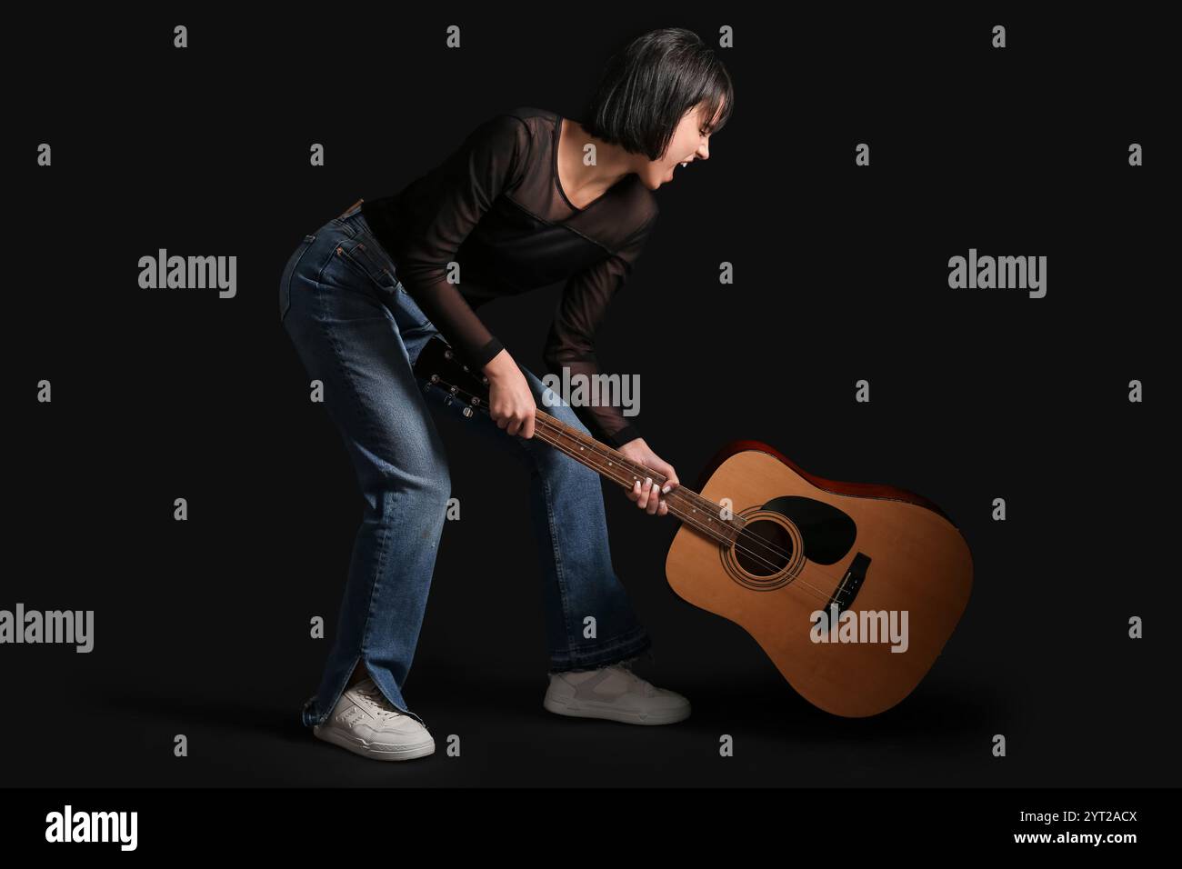 Young woman smashing guitar on black background Stock Photo - Alamy