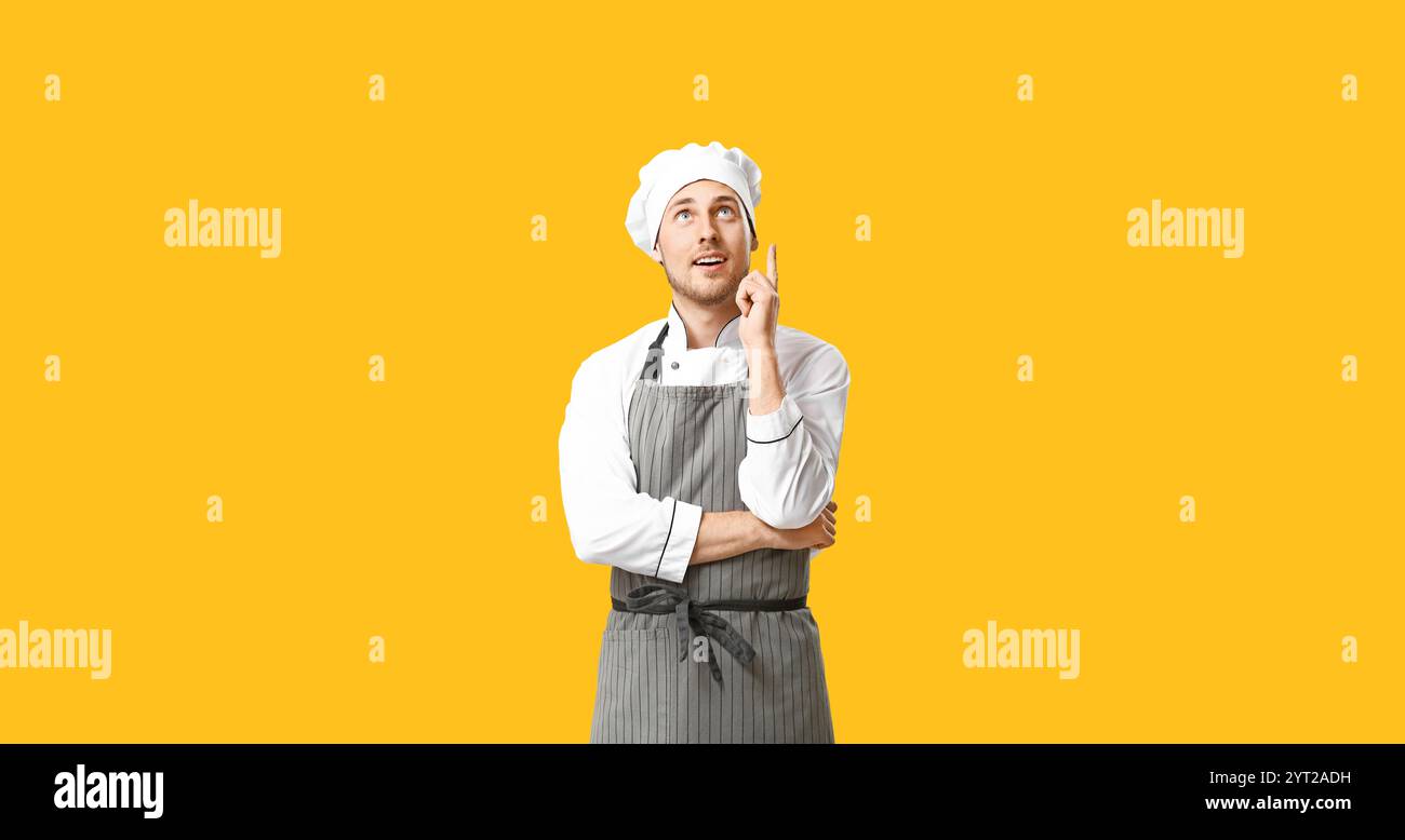 Handsome male chef pointing upwards on yellow background Stock Photo ...