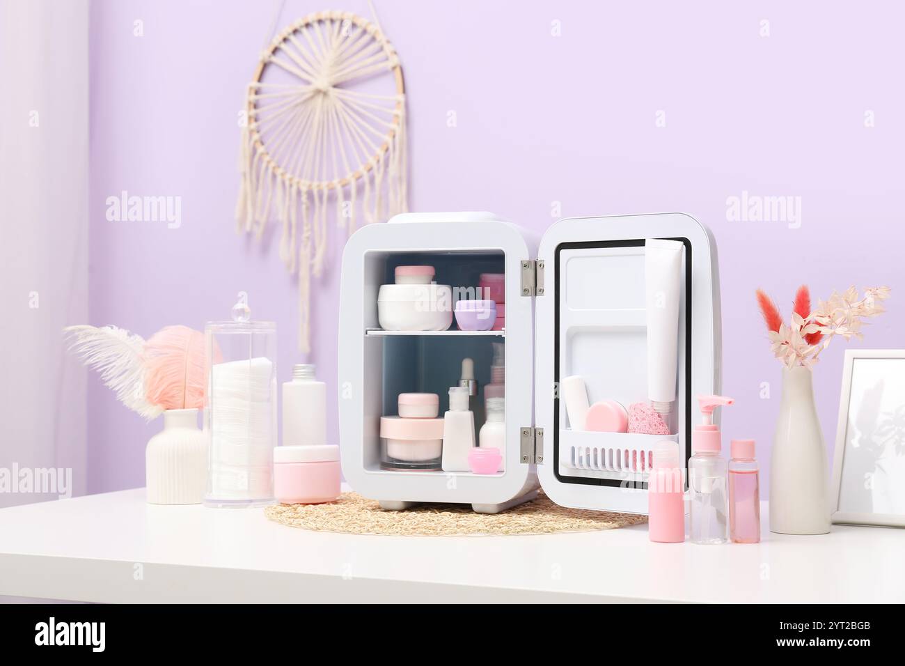 Small refrigerator with cosmetic products on table against lilac wall ...