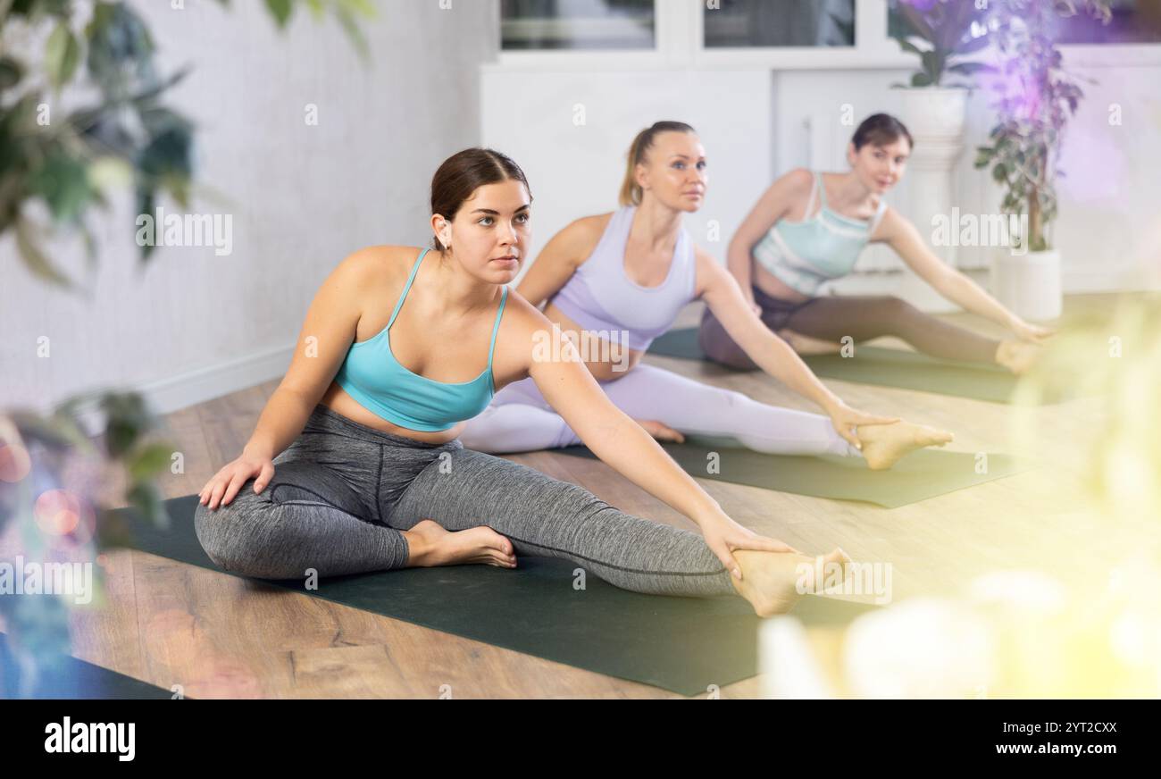 Calm sporty women stretching in Janu Sirsasana and bending head to knee ...