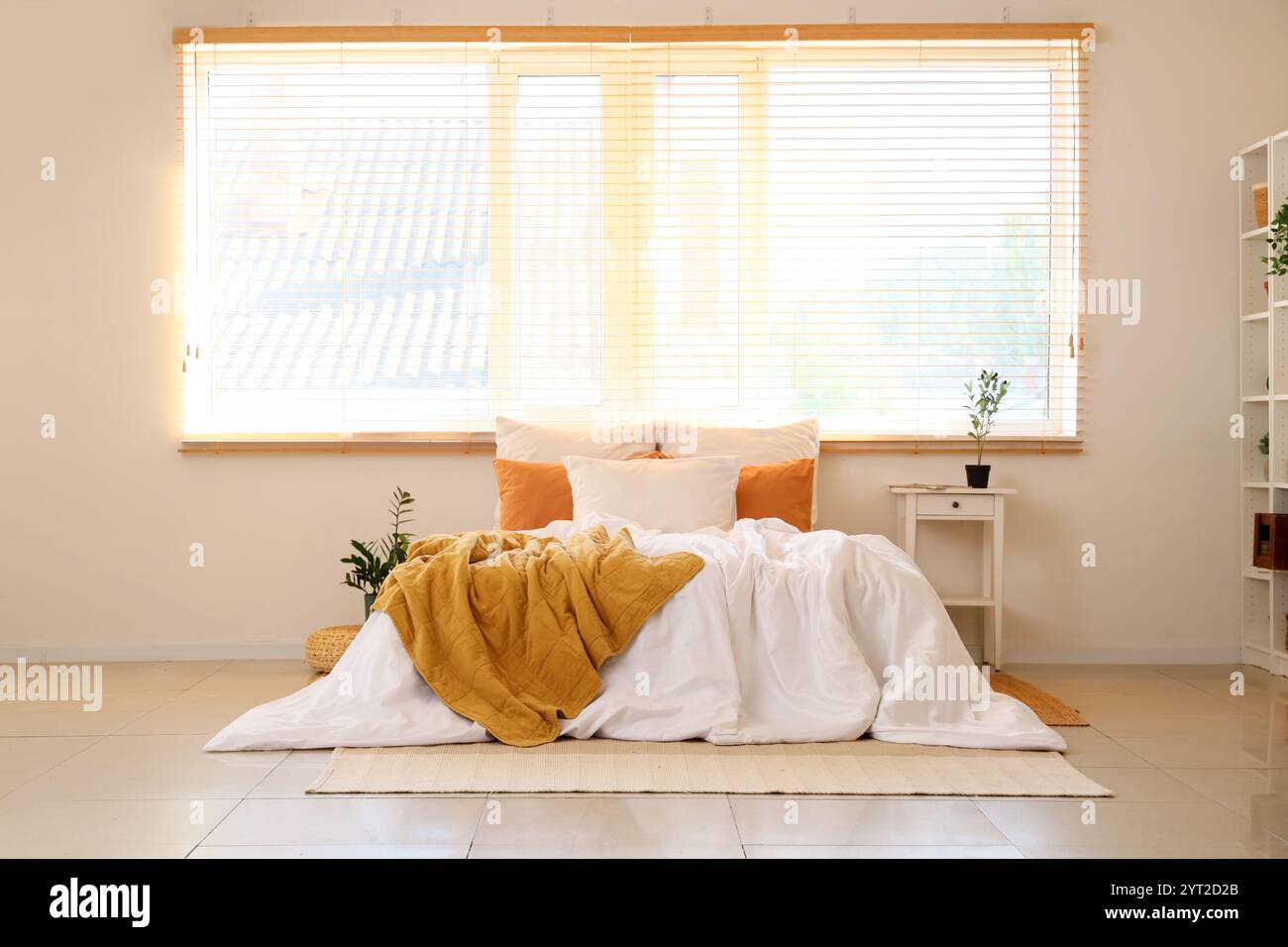 Big comfortable bed with crumpled linen, bedside table and houseplants ...