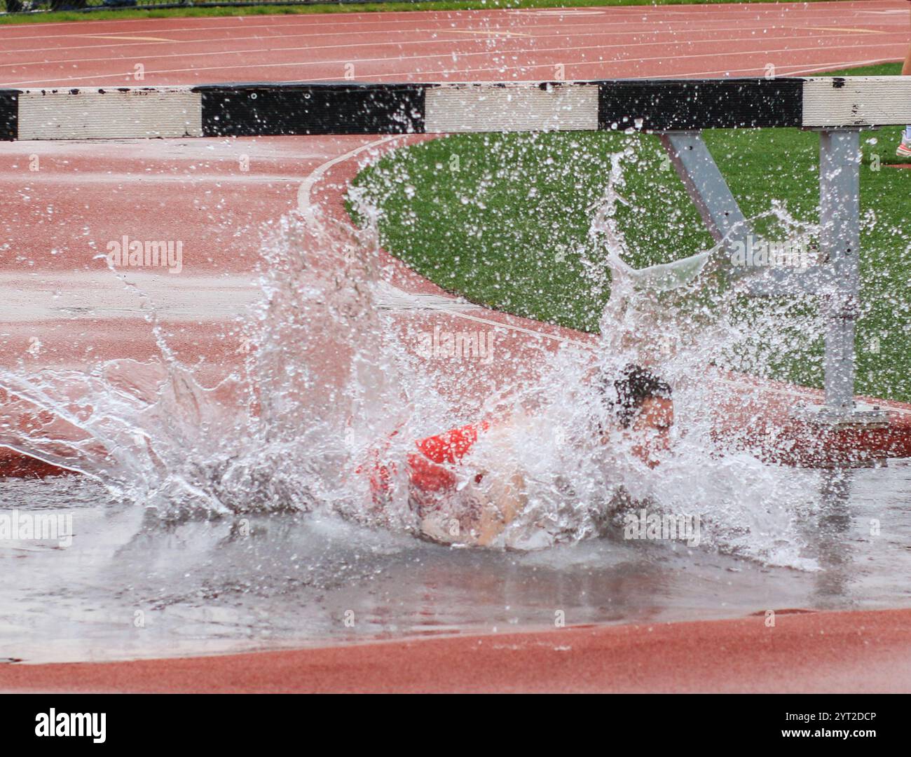A competitor splashes into a water pit while tackling a hurdle at a ...