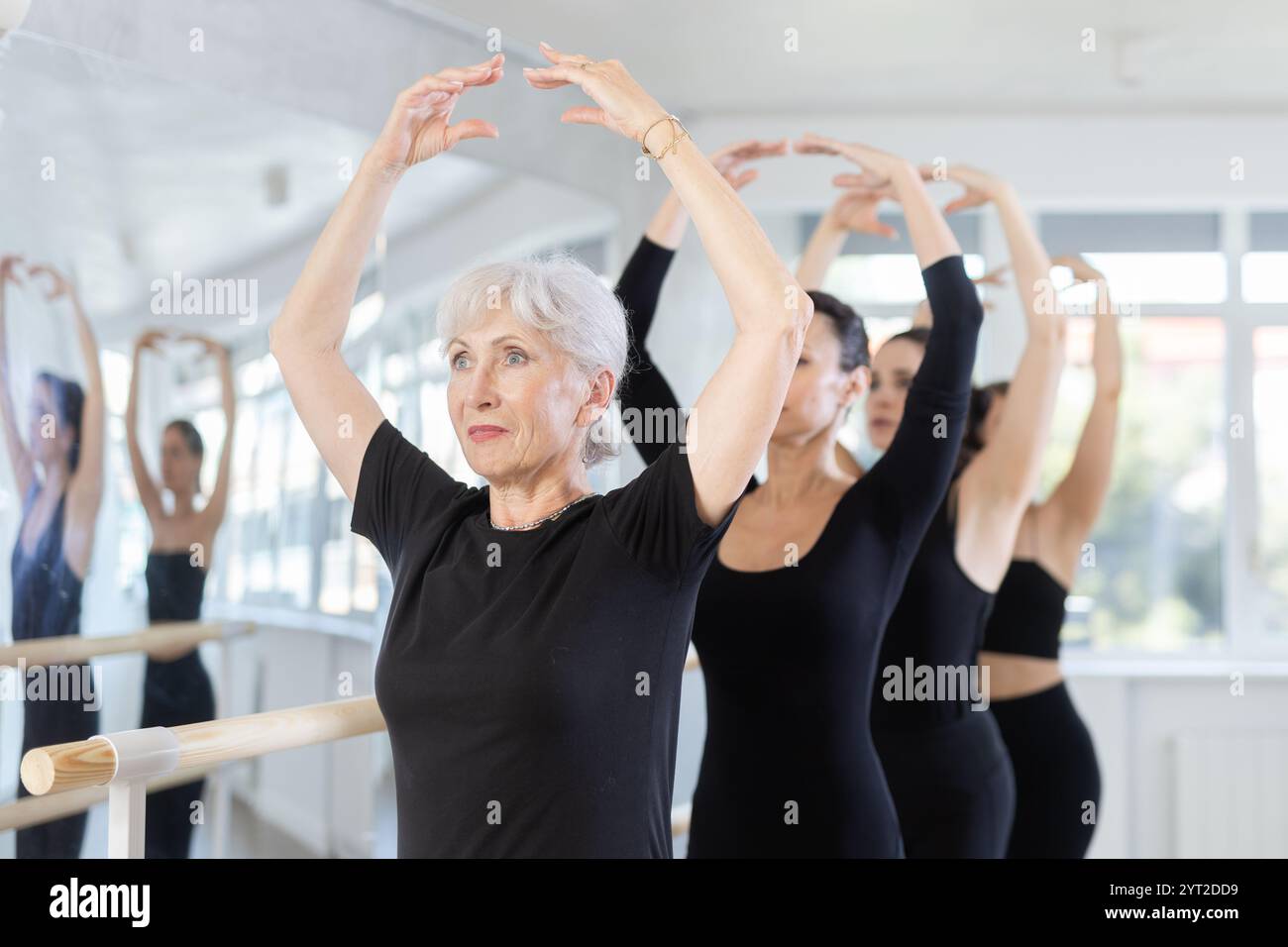 Female ballet dancers doing various ballet movements at ballet barre in ...