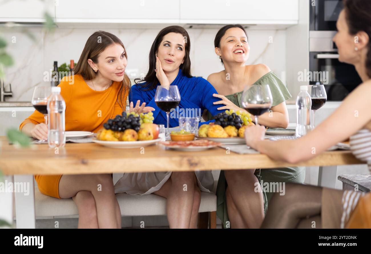 Girlfriends drinking wine and having conversation over dinner at house ...