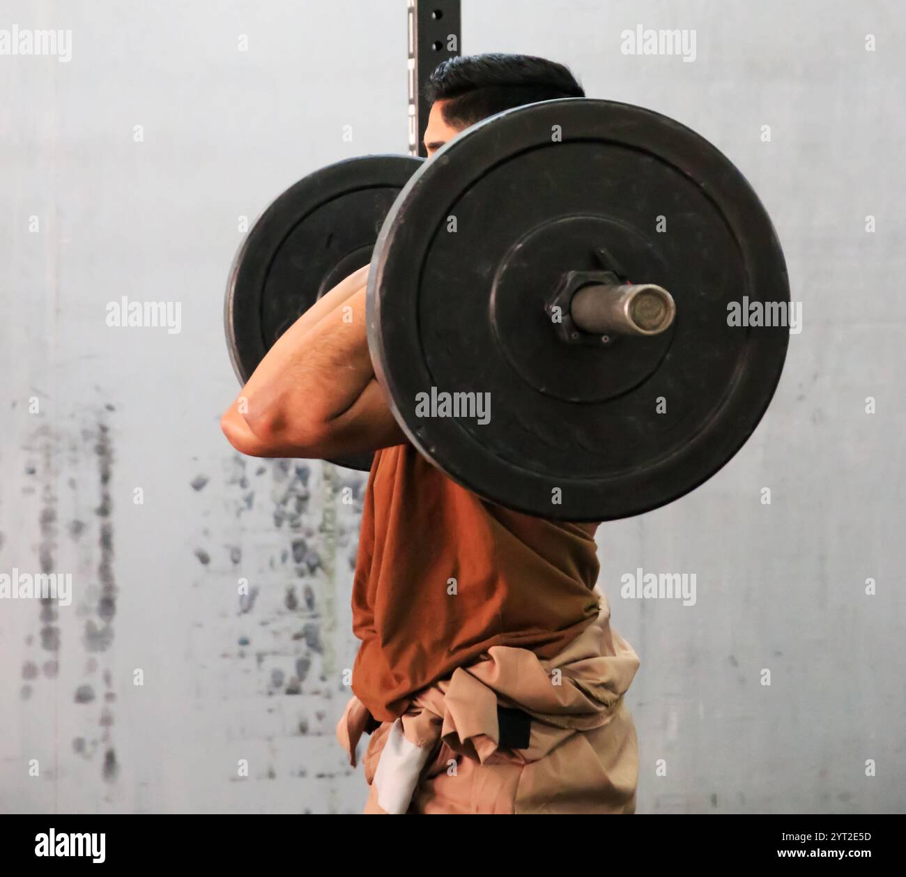 A person performs a barbell lift while working out at a gym, focusing ...