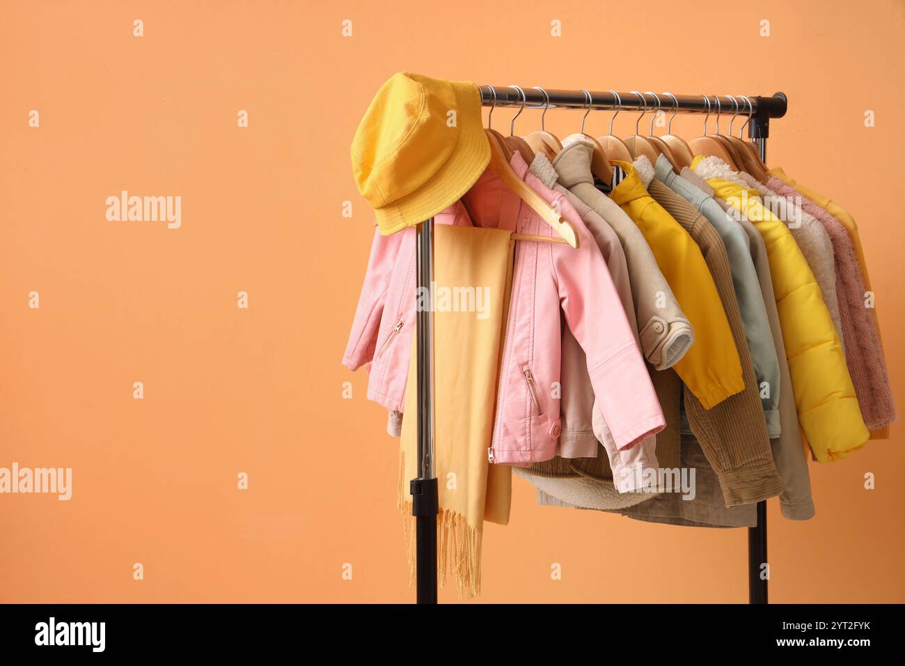 Rack with stylish children's clothes and accessories on orange ...
