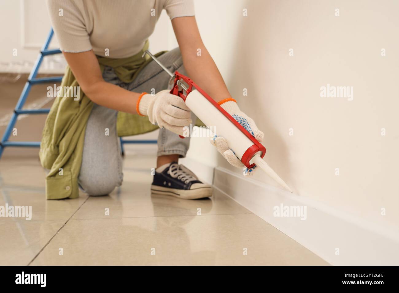 Young woman applying sealant to baseboard in room Stock Photo - Alamy
