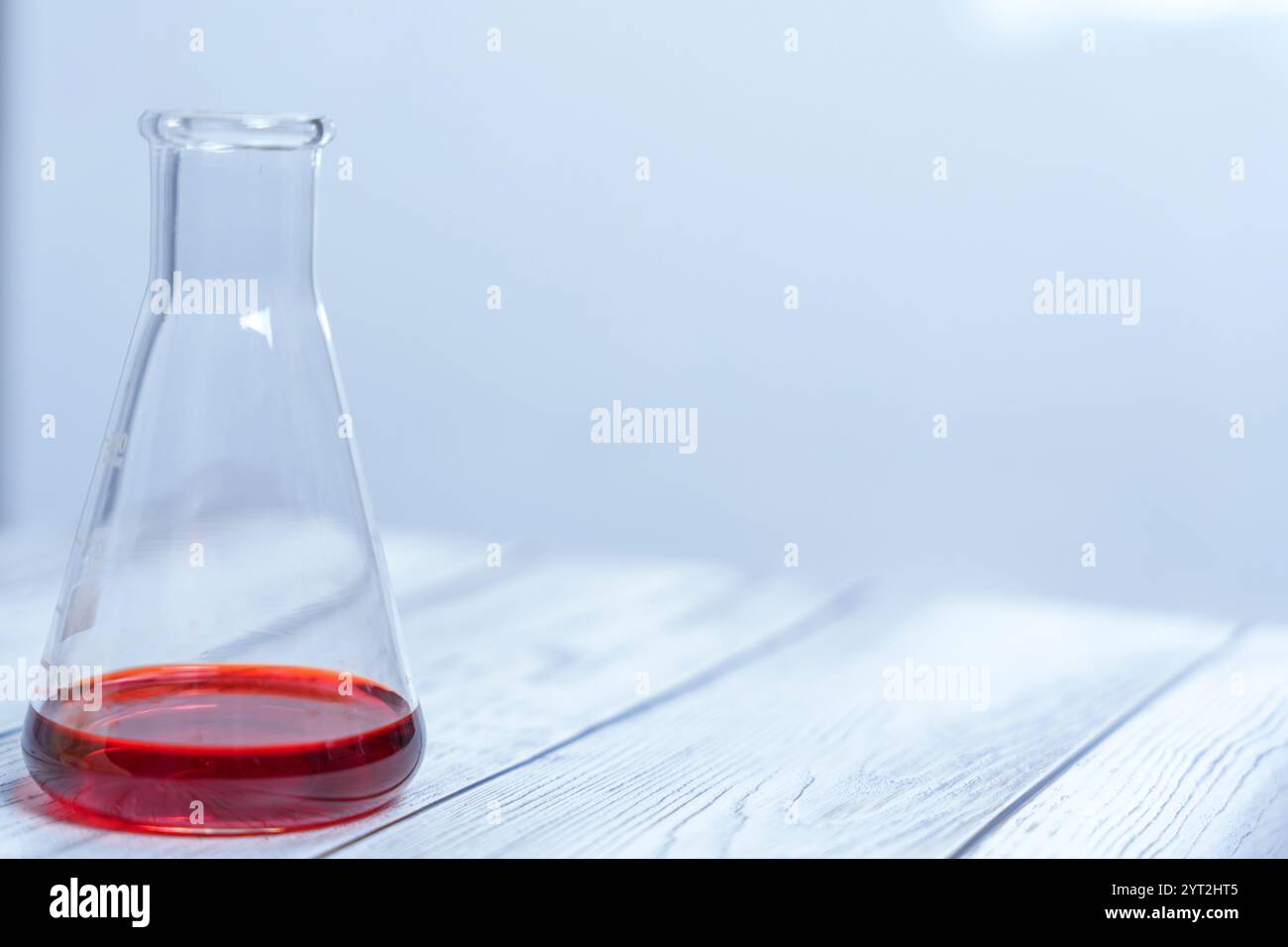 A glass Erlenmeyer flask with red liquid on a white surface. Scientific ...