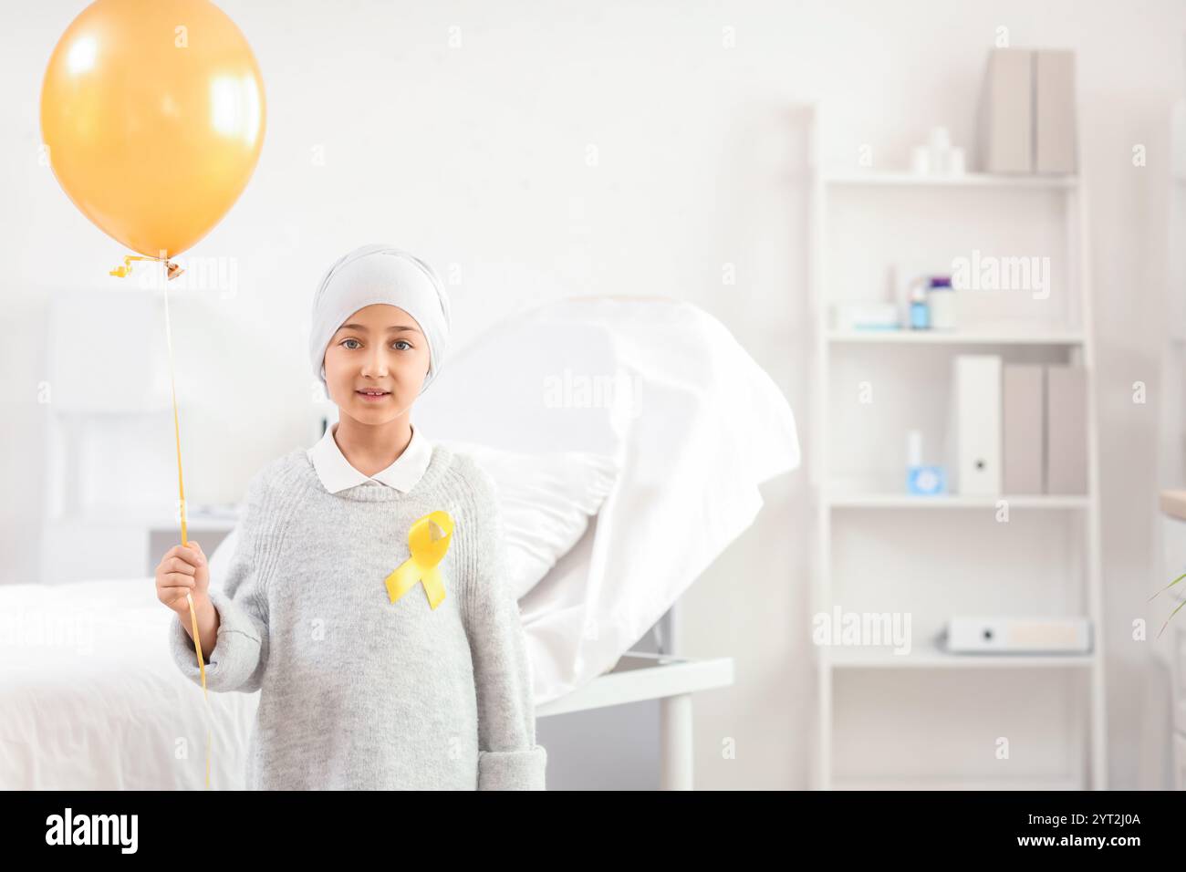 Little girl after chemotherapy with yellow ribbon and balloon in clinic ...