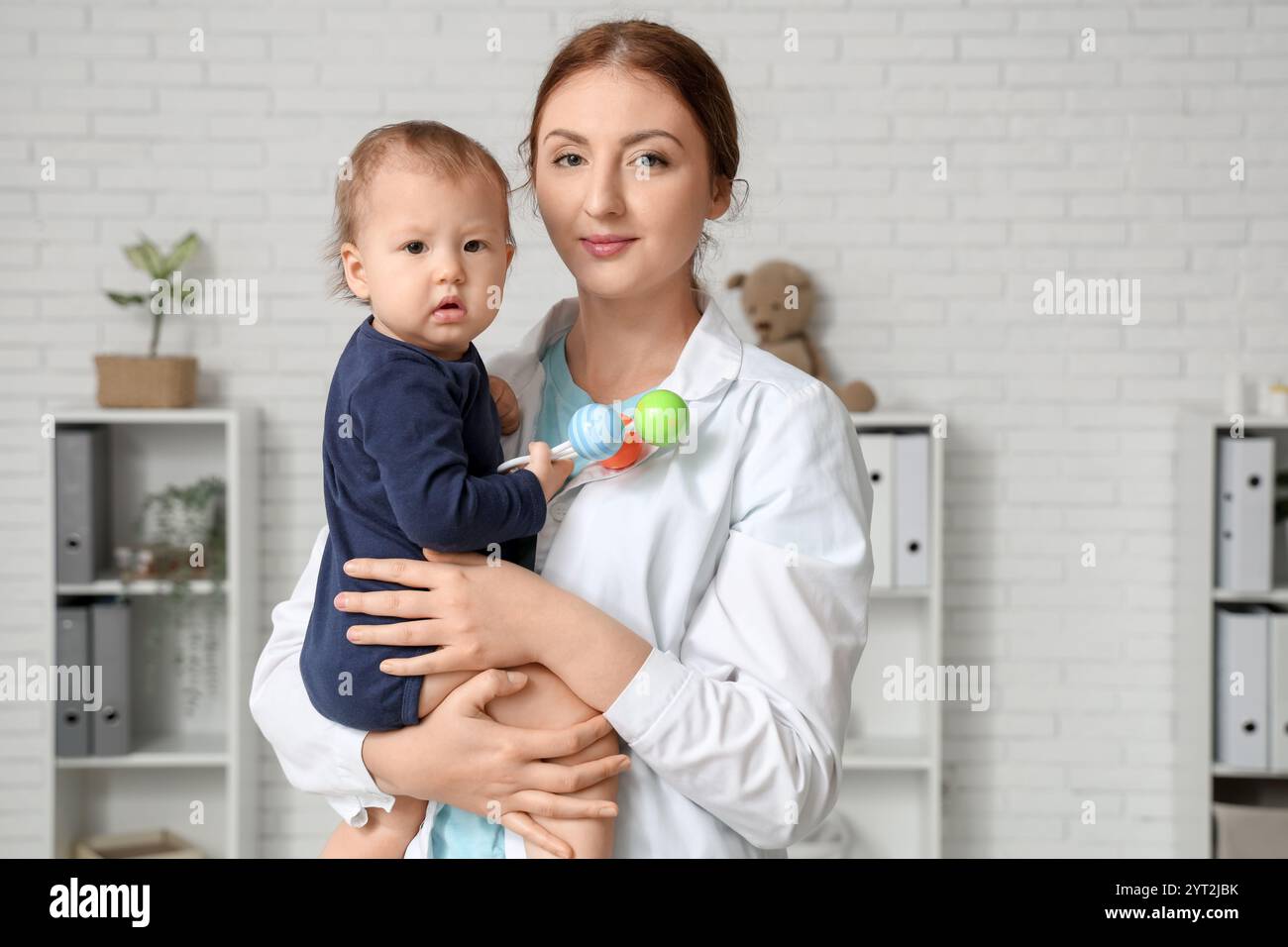 Young happy female pediatrician with cute little baby and rattle in ...