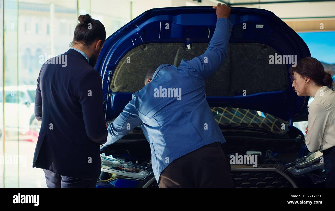 Customers in car showroom looking at components under vehicle hood ...