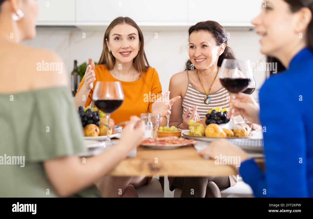 Girlfriends drinking wine and having conversation over dinner at house ...