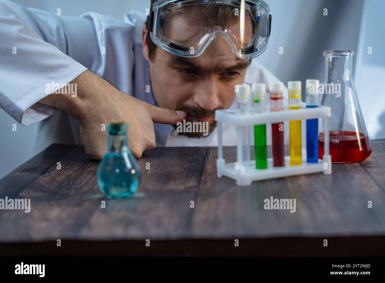 A scientist wearing protective goggles examines a round-bottom flask ...