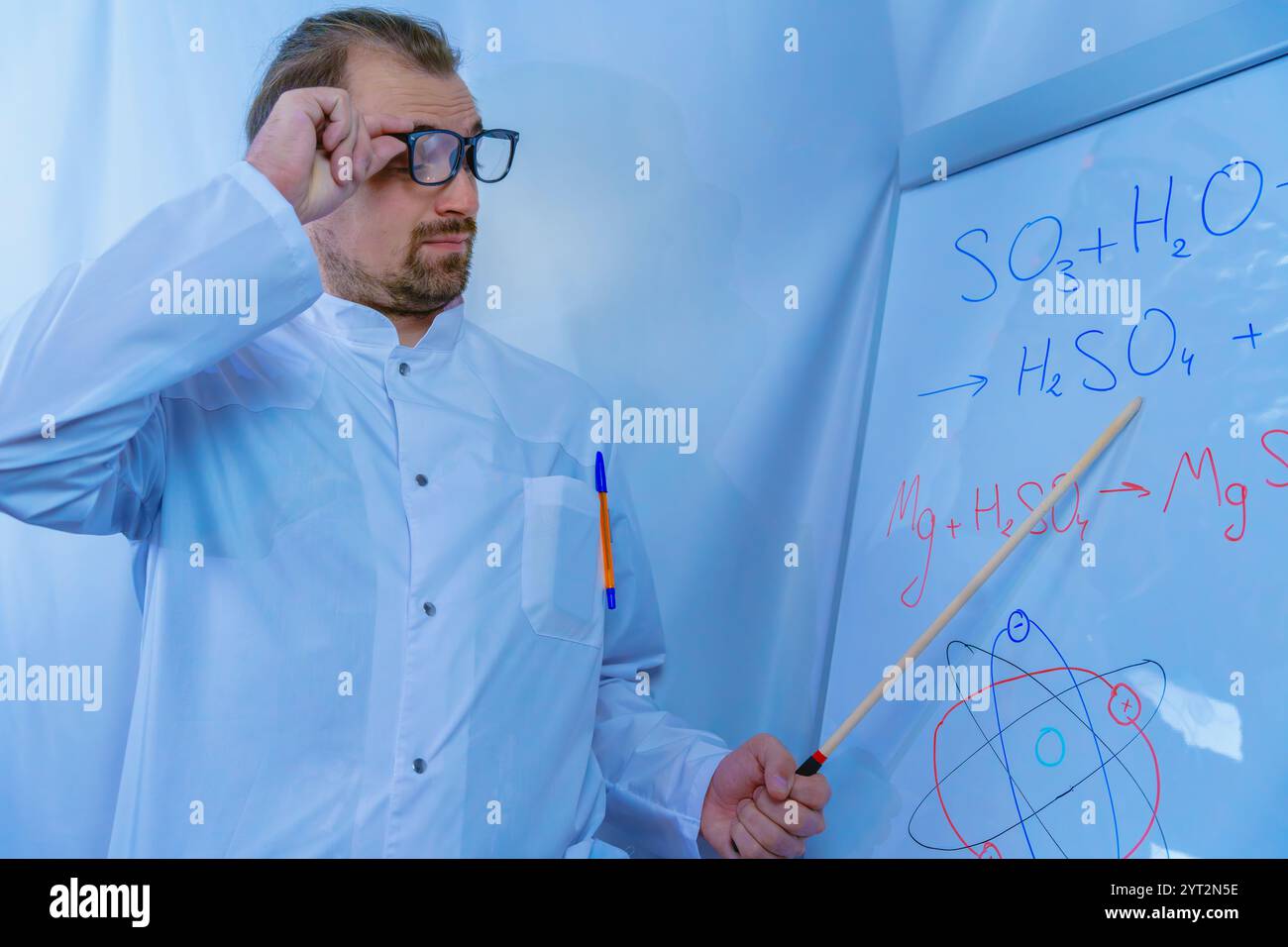 A scientist in a lab coat and glasses pointing at chemical formulas on ...