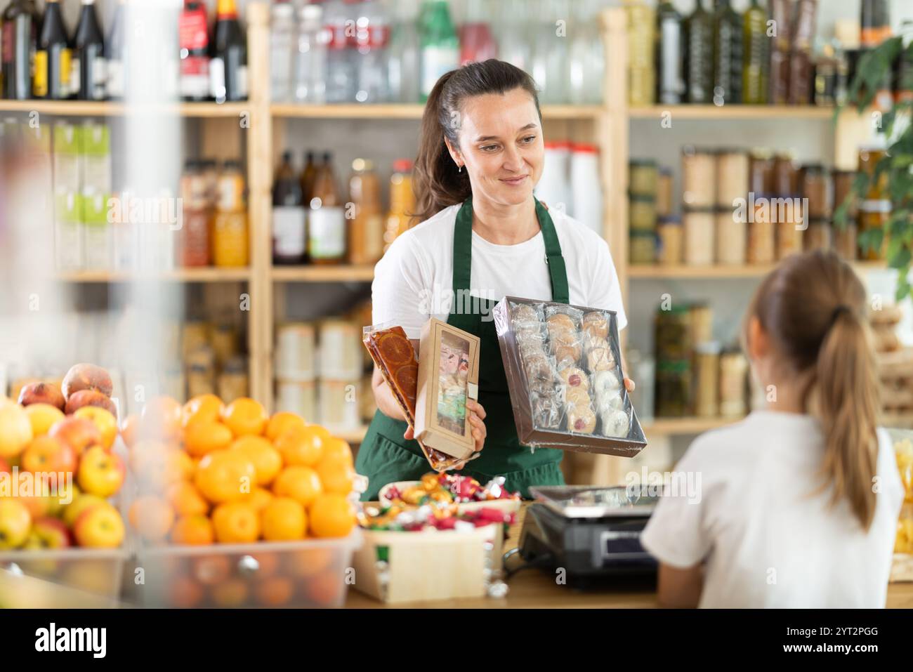 Woman sells sweets to girl, offer and show nougat and cookies Stock ...