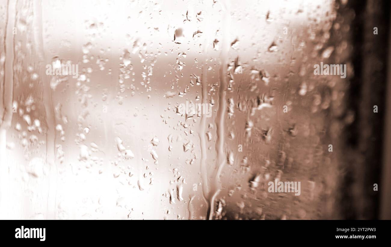Macro of water drops on glass. Large rain drops strike window during winter shower. Colour of ...