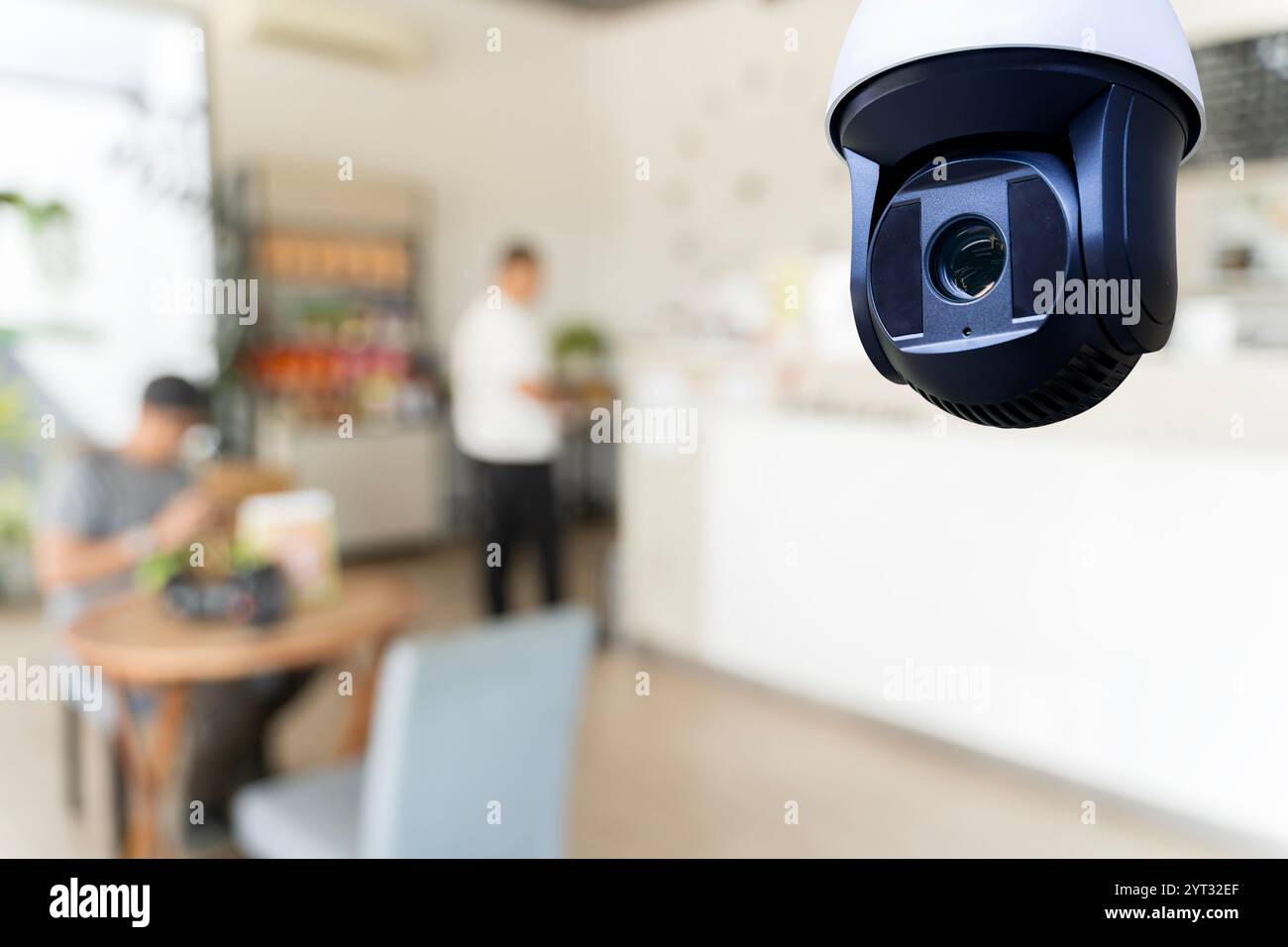 A security camera hangs from the ceiling of a cafe, with the interior ...