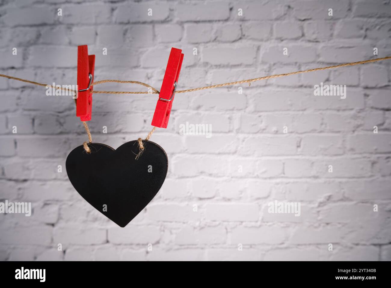 Black heart hanging on string with red clothespins, brick wall ...