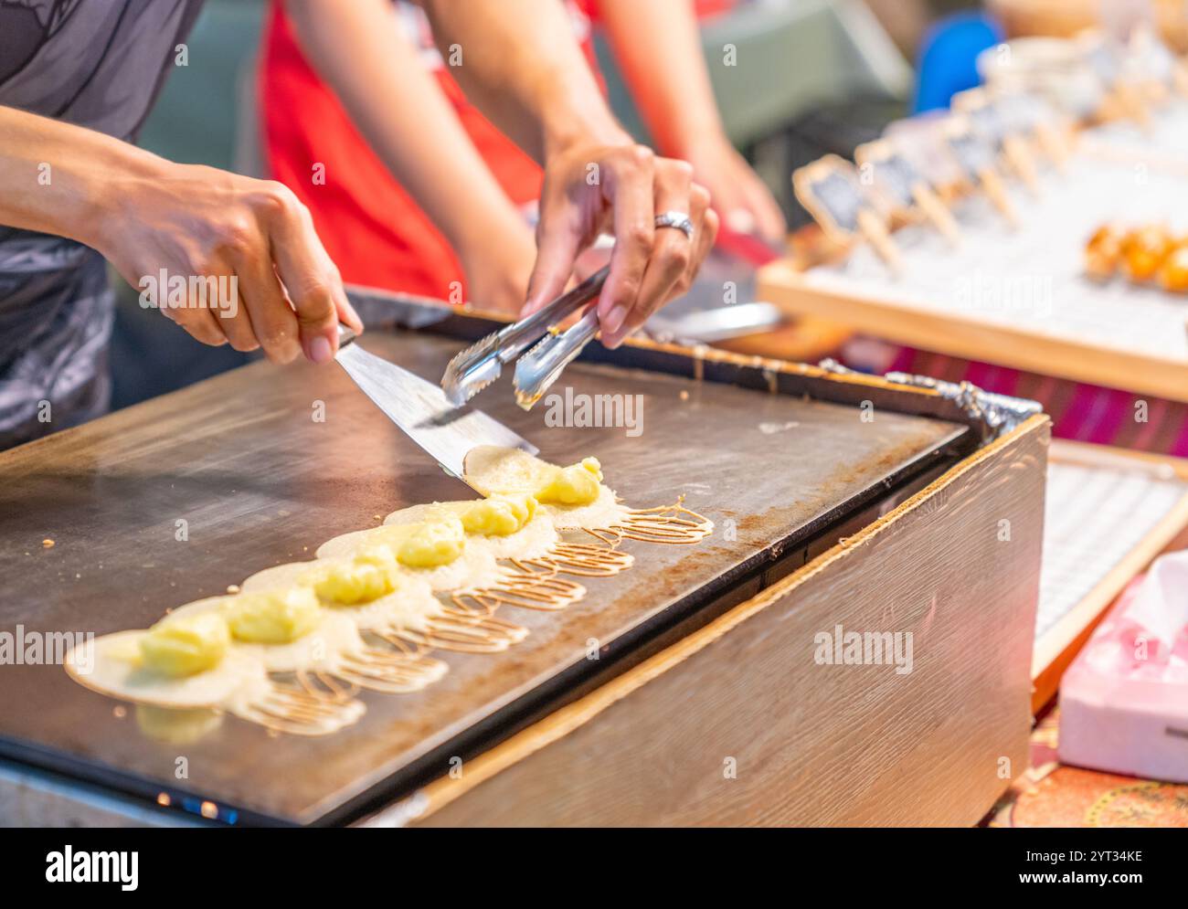 The vendor is using a spatula and tongs to flip the Tokyo pancake on ...