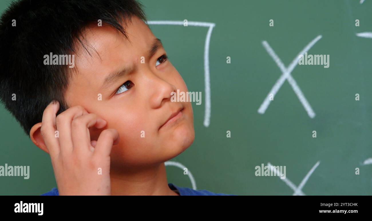 Front view of thoughtful Asian schoolboy scratching his head against ...