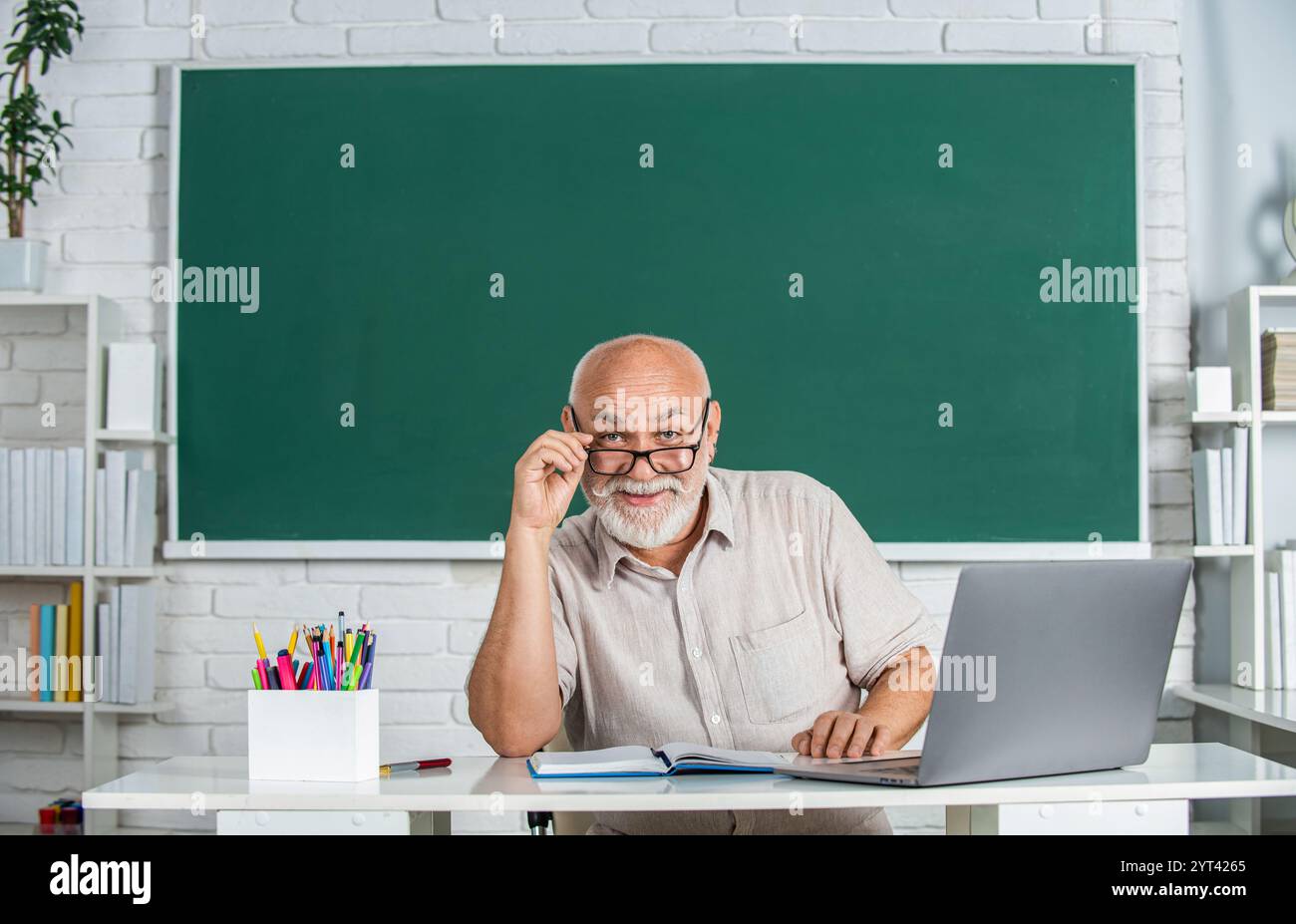 Old male teacher in front of blackboard. Man teacher sitting in front ...
