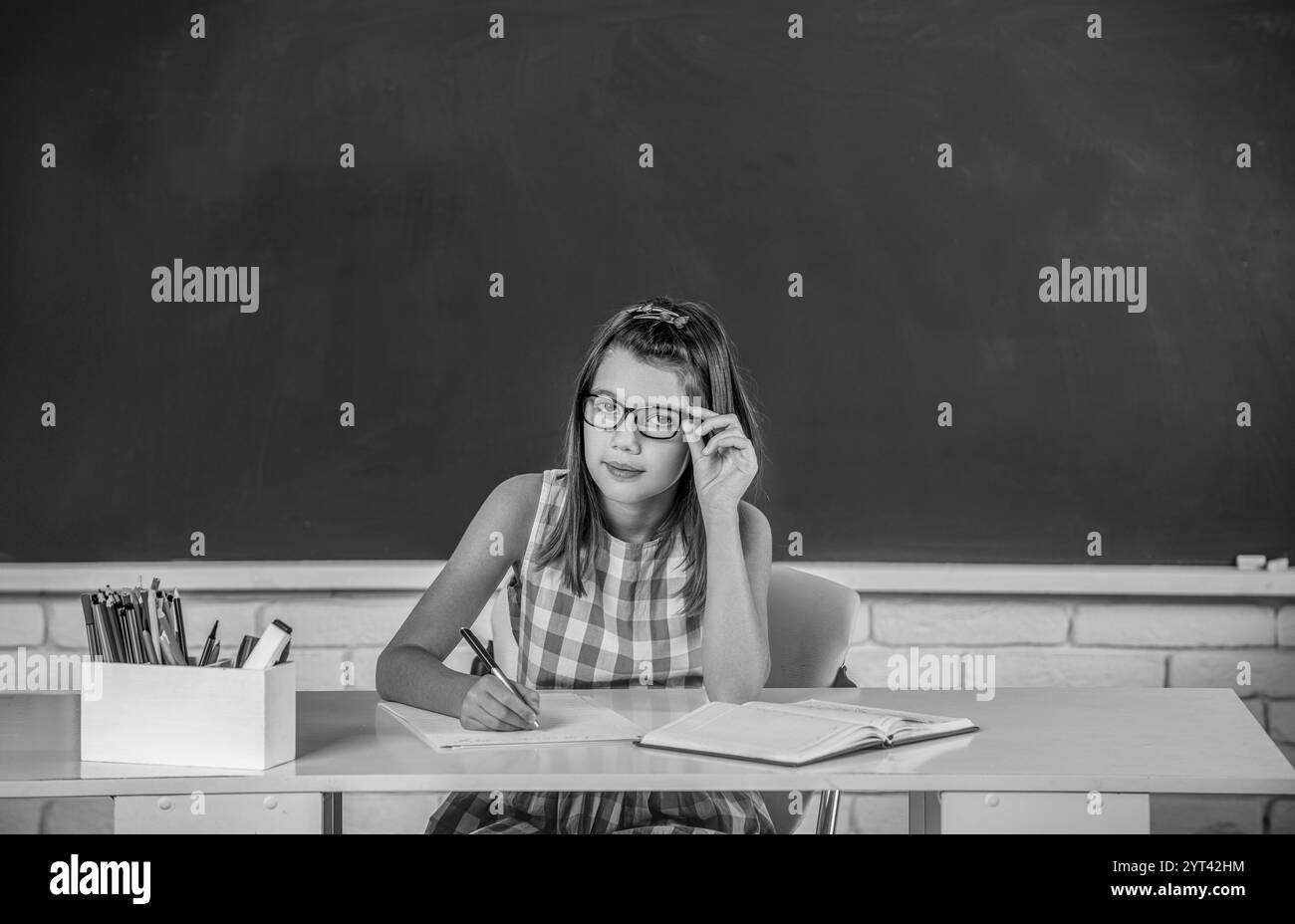 Smiling cute schoolgirl with in classroom on chalkboard blackboard ...