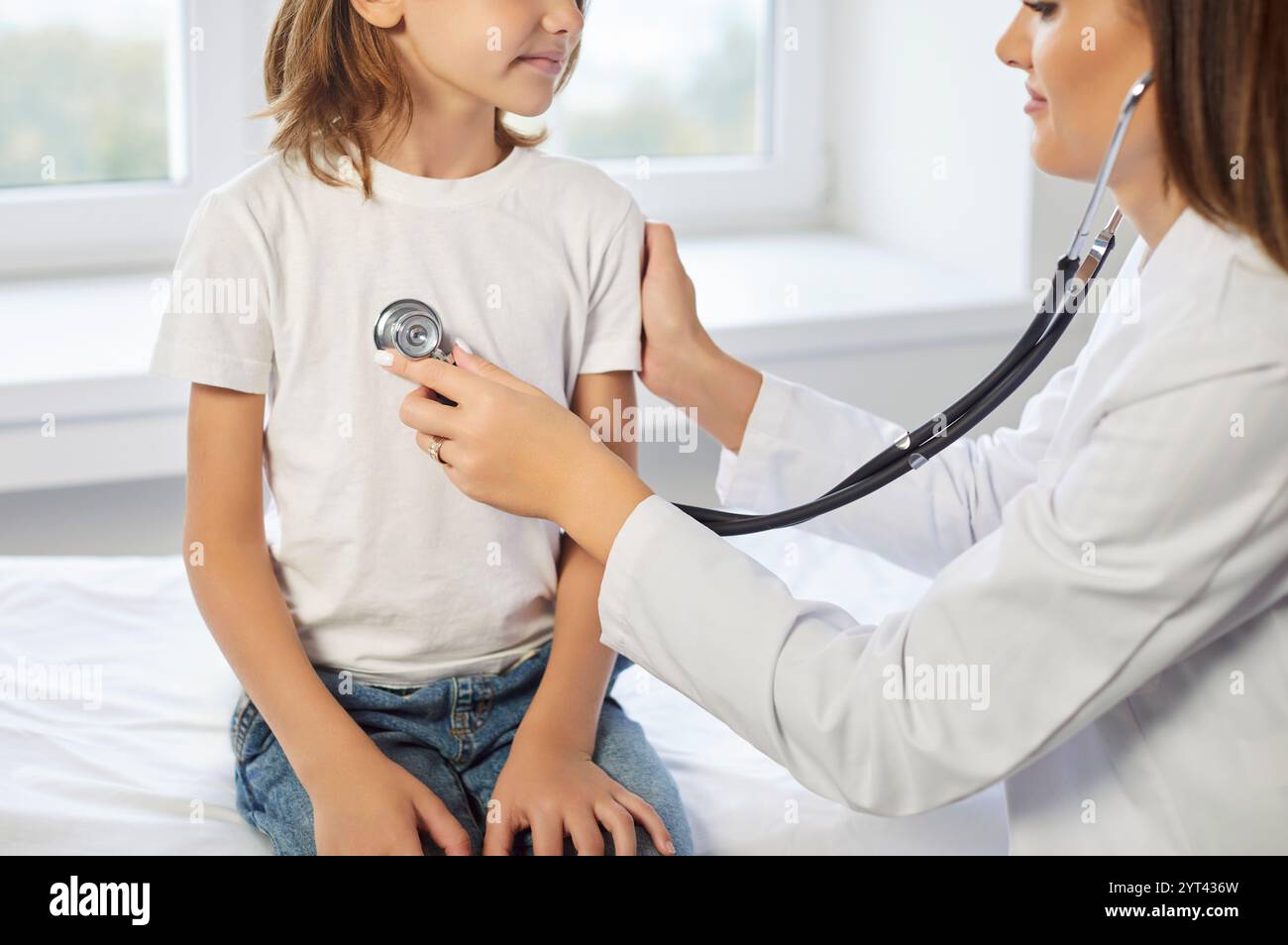 Caring kind woman doctor holding stethoscope listening to small boy patient heart chest in ...