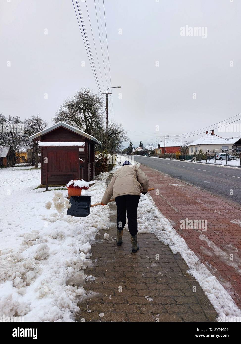 female villager clearing snow away with shovel from village footpath ...