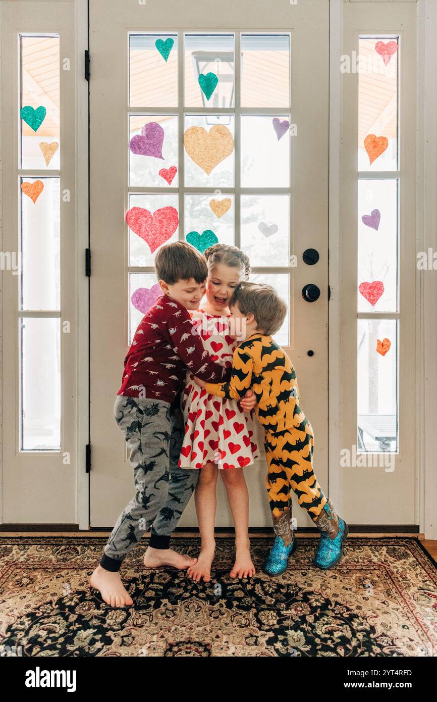 Three siblings hug and laugh together near heart-decorated doors Stock ...