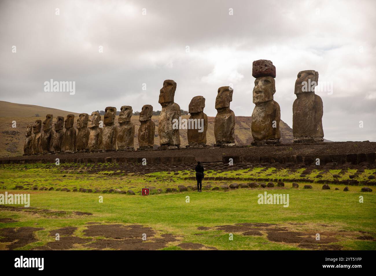 A tourist gazes at the iconic Easter Island statues under a cloudy sky ...