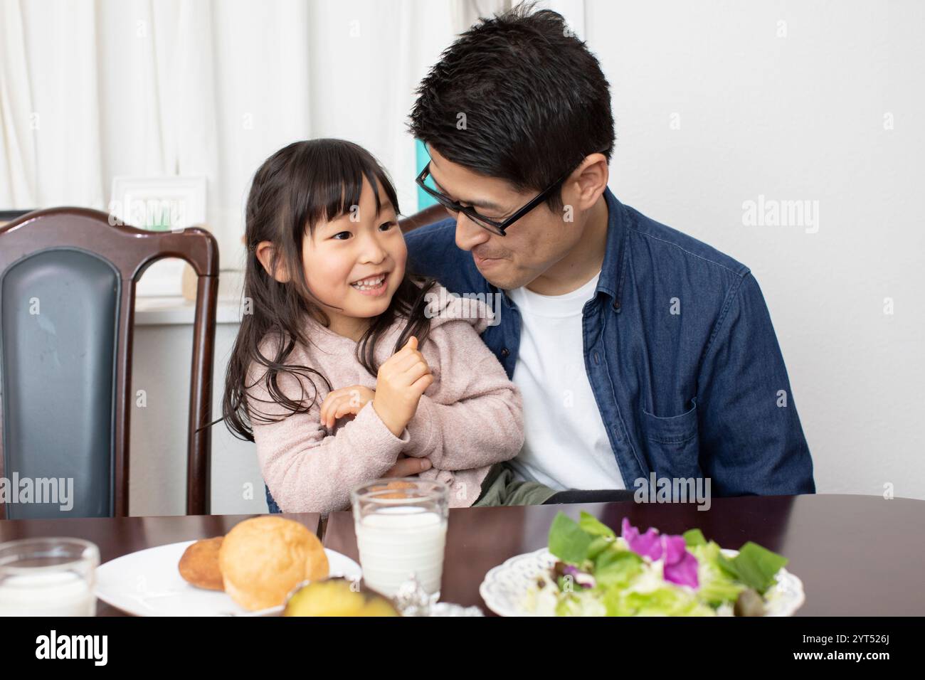 Girl sitting on father's lap eating a meal Stock Photo - Alamy