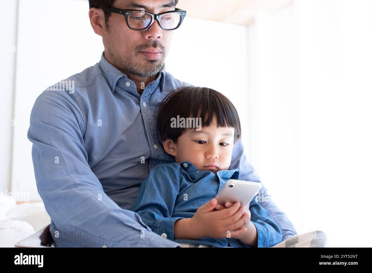 Boy looking at phone on father's lap Stock Photo - Alamy