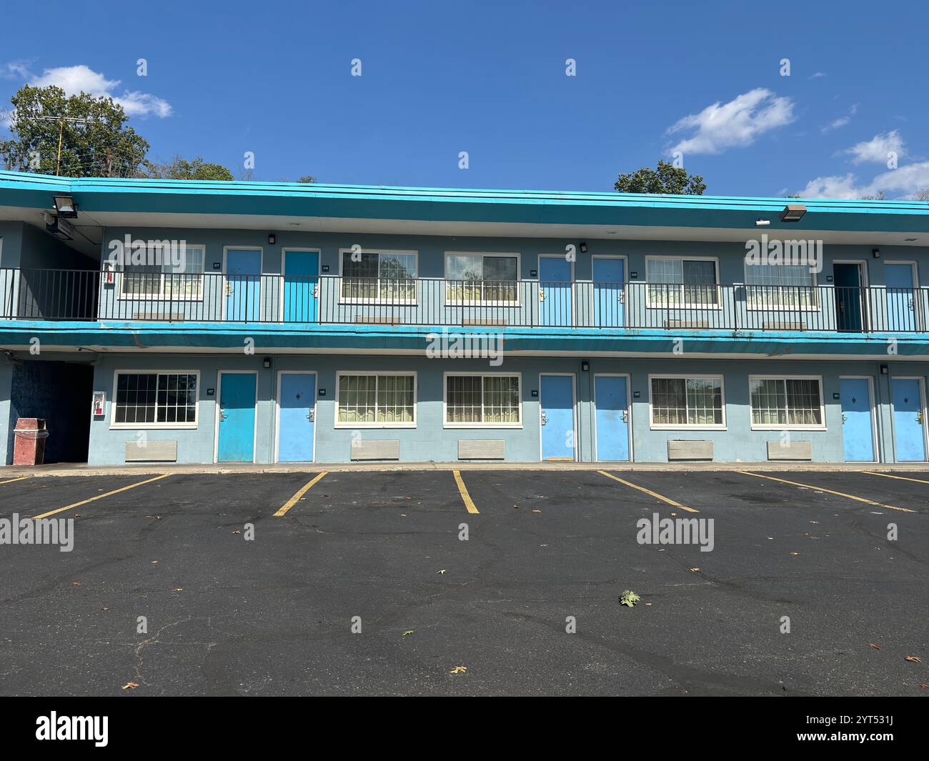 Two-story blue motel exterior with parking lot under a clear blue sky ...