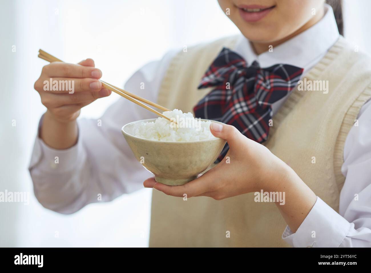 Female student holding a tea bowl and eating rice Stock Photo - Alamy