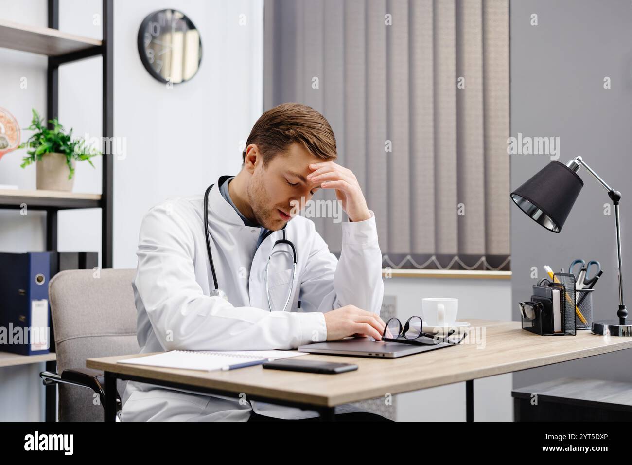 Handsome doctor man wearing medical uniform sitting on his workplace ...