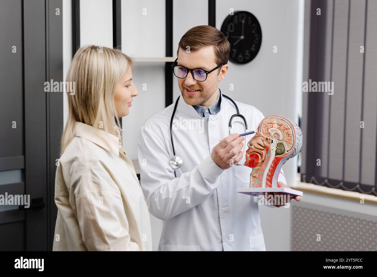 A young attractive otolaryngologist doctor shows a model of the human ...
