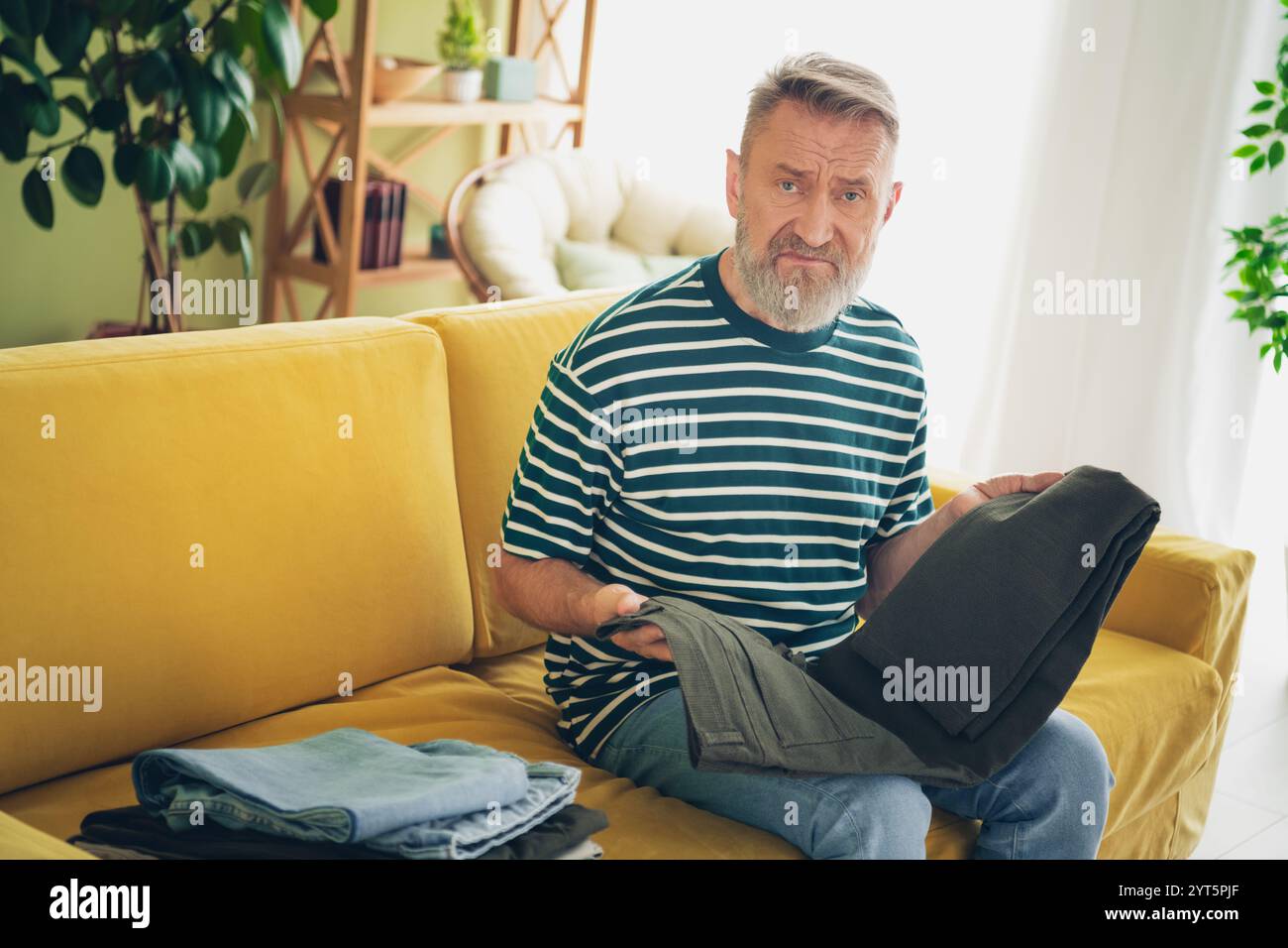 Elderly man relaxes at home holding folded garments in comfortable and ...