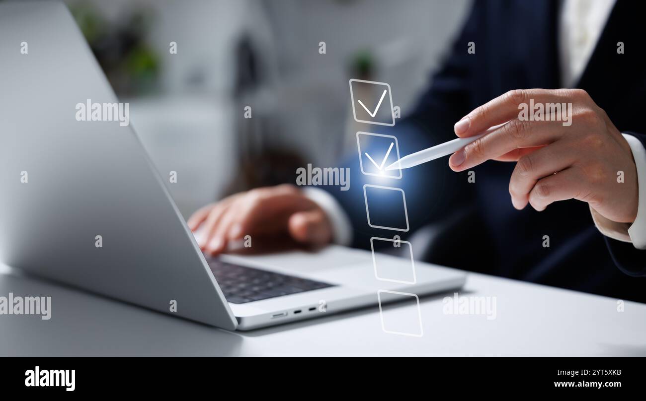 A businessman sits at his laptop, using a pen to check off completed ...