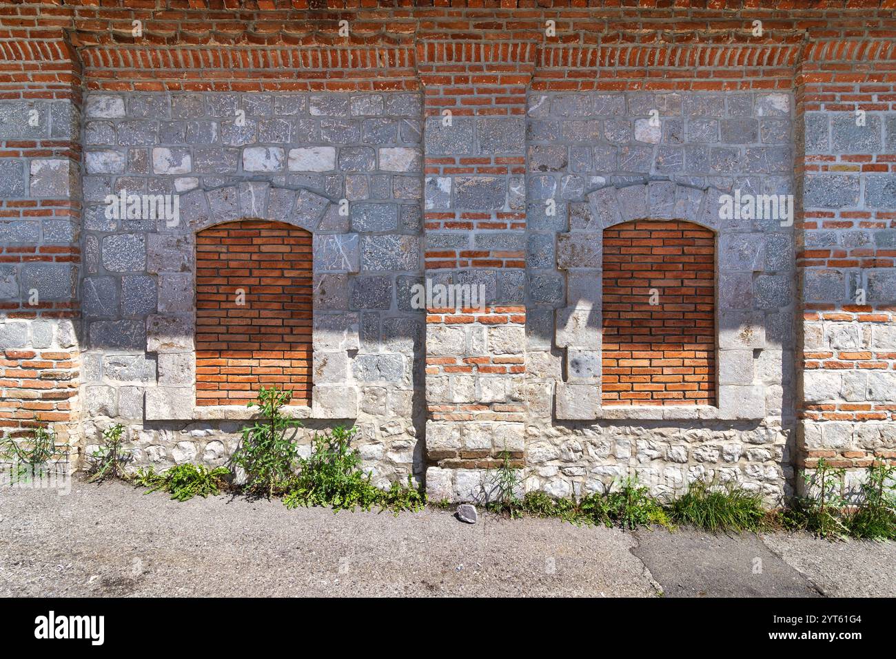 Brick wall with two arched windows. The wall is made of a combination ...