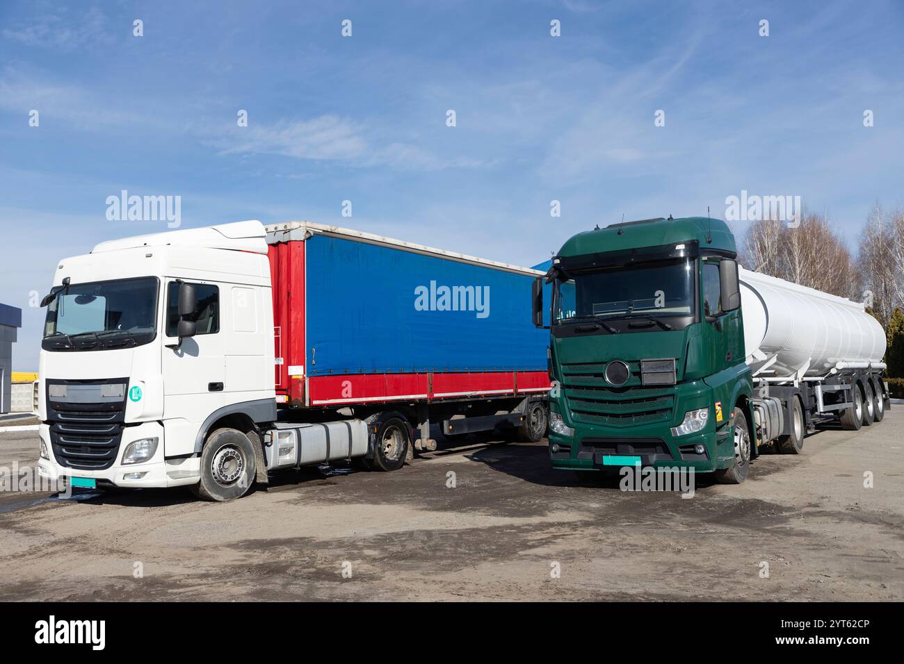 Two ten-wheeler trucks, one with a tank trailer, parked in the parking ...