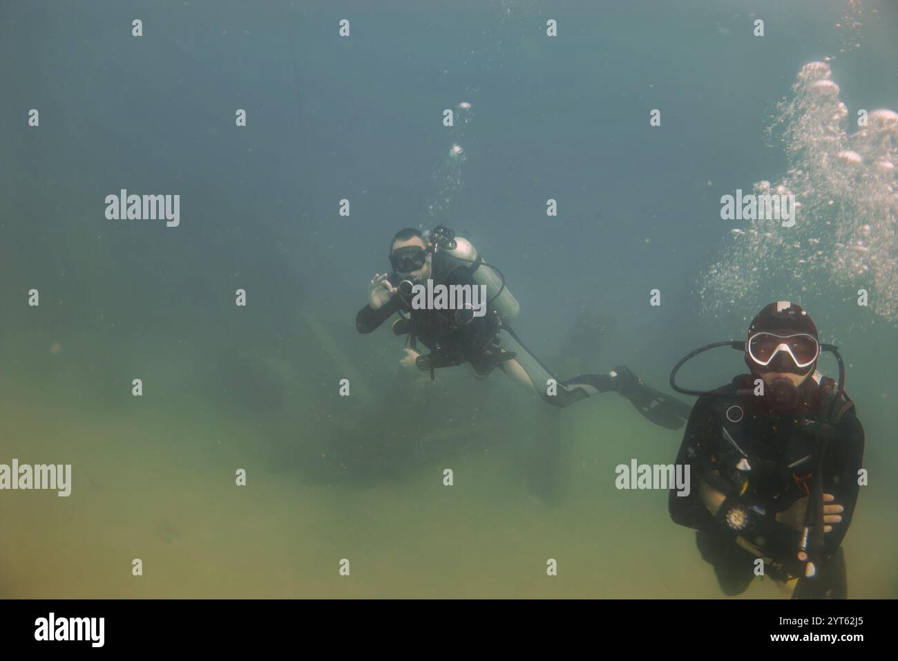 Two divers are exploring murky waters, navigating through a challenging ...
