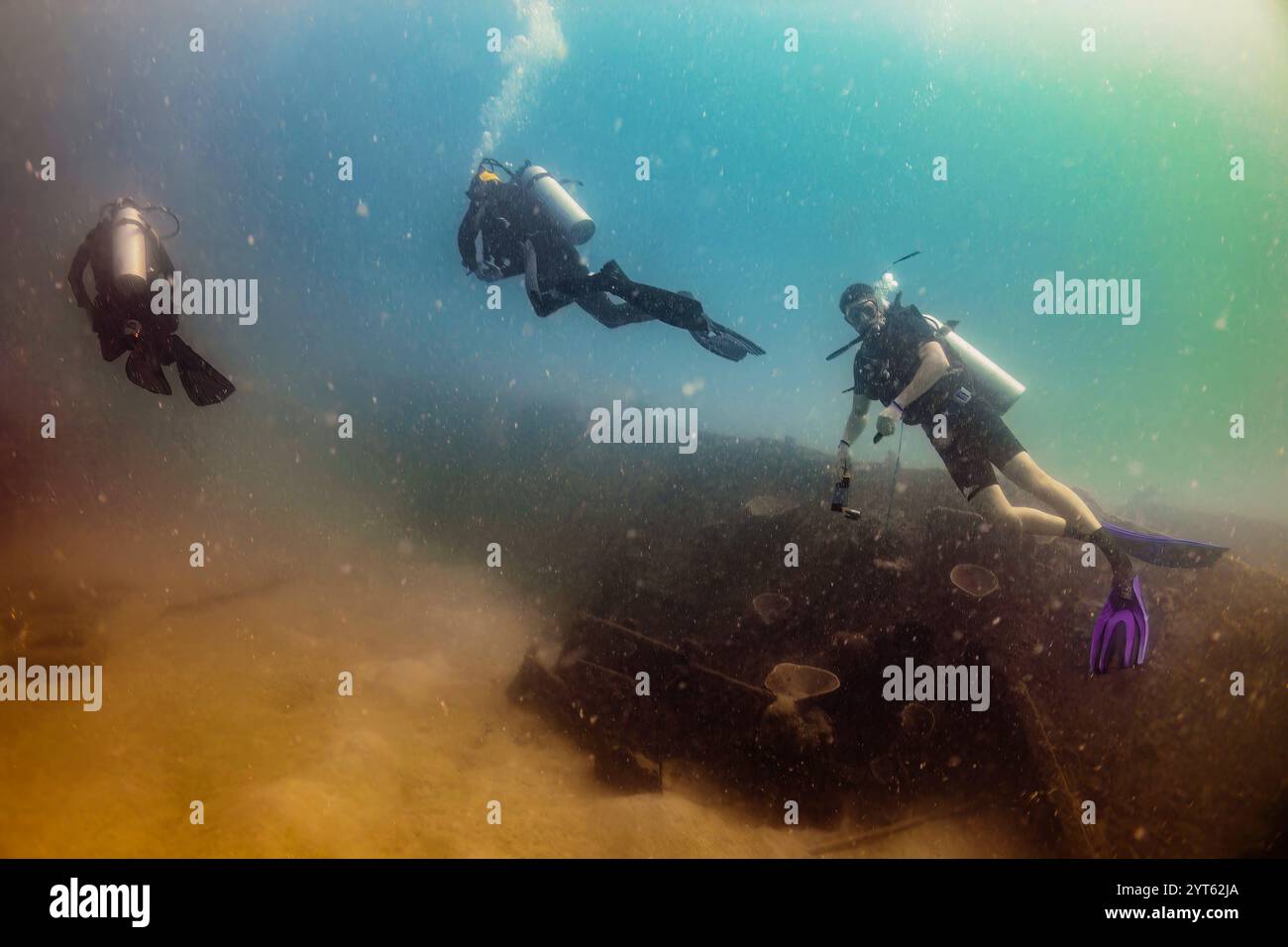 Three divers navigating through a muddy shipwreck in the deep ocean ...