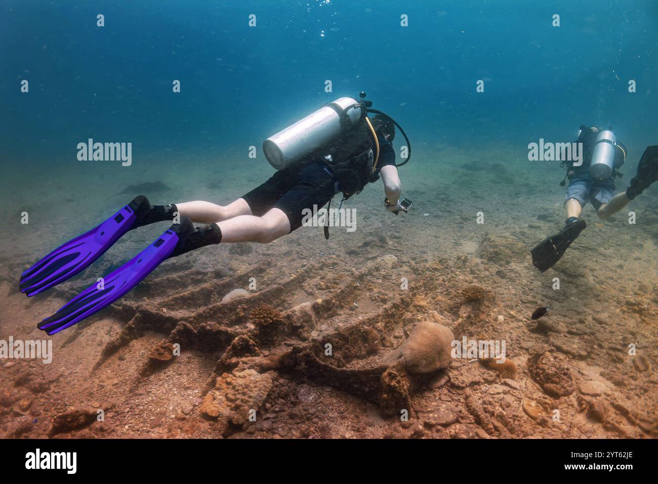Two scuba divers are exploring the deteriorated skeleton of a shipwreck ...