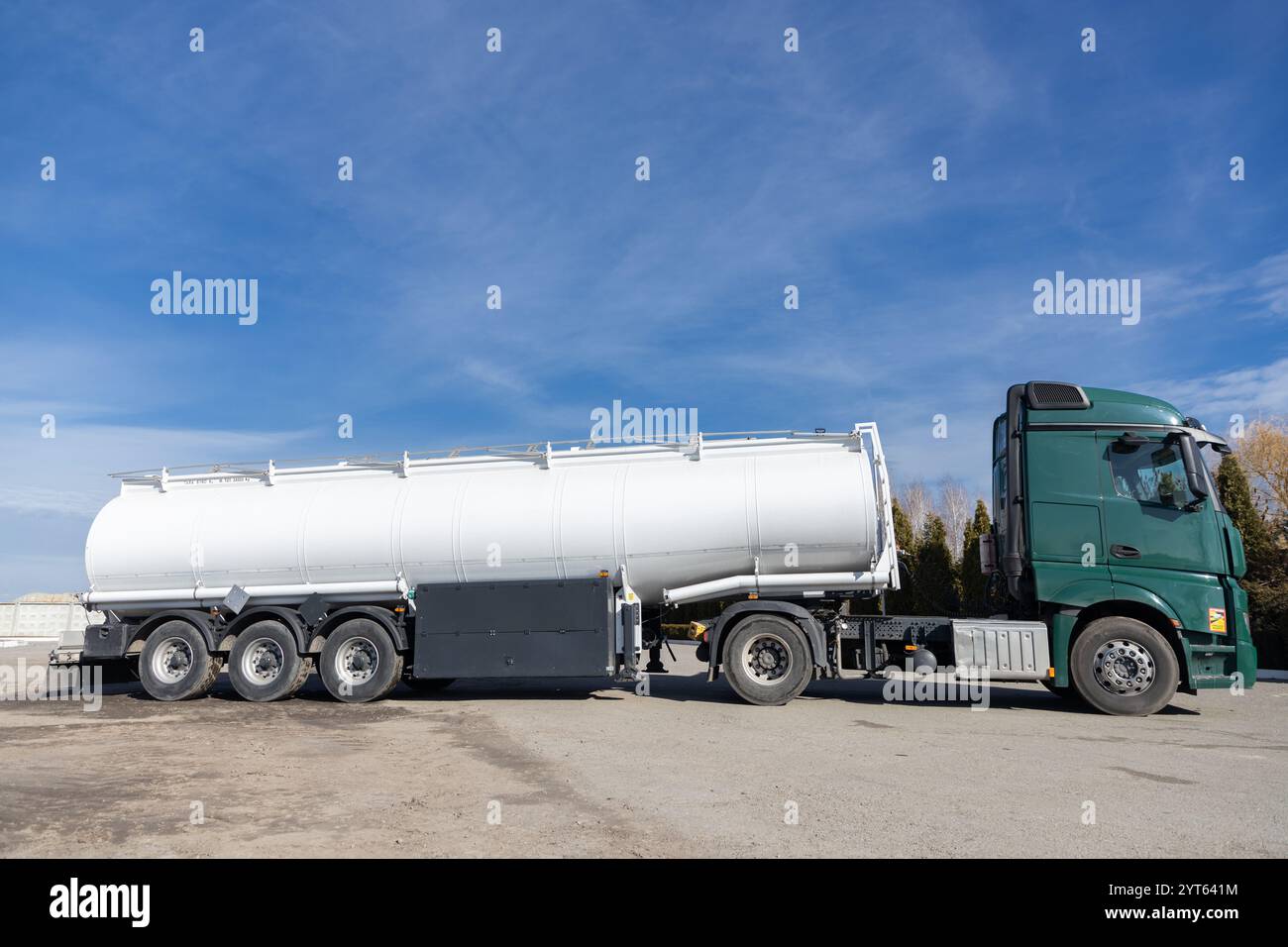 Green cab with tank trailer standing on asphalt under blue sunny sky ...
