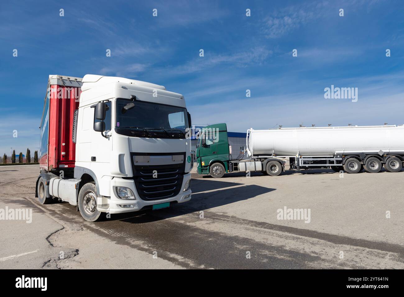 Two long ten-wheel trucks, one with a tank trailer, park in the parking ...