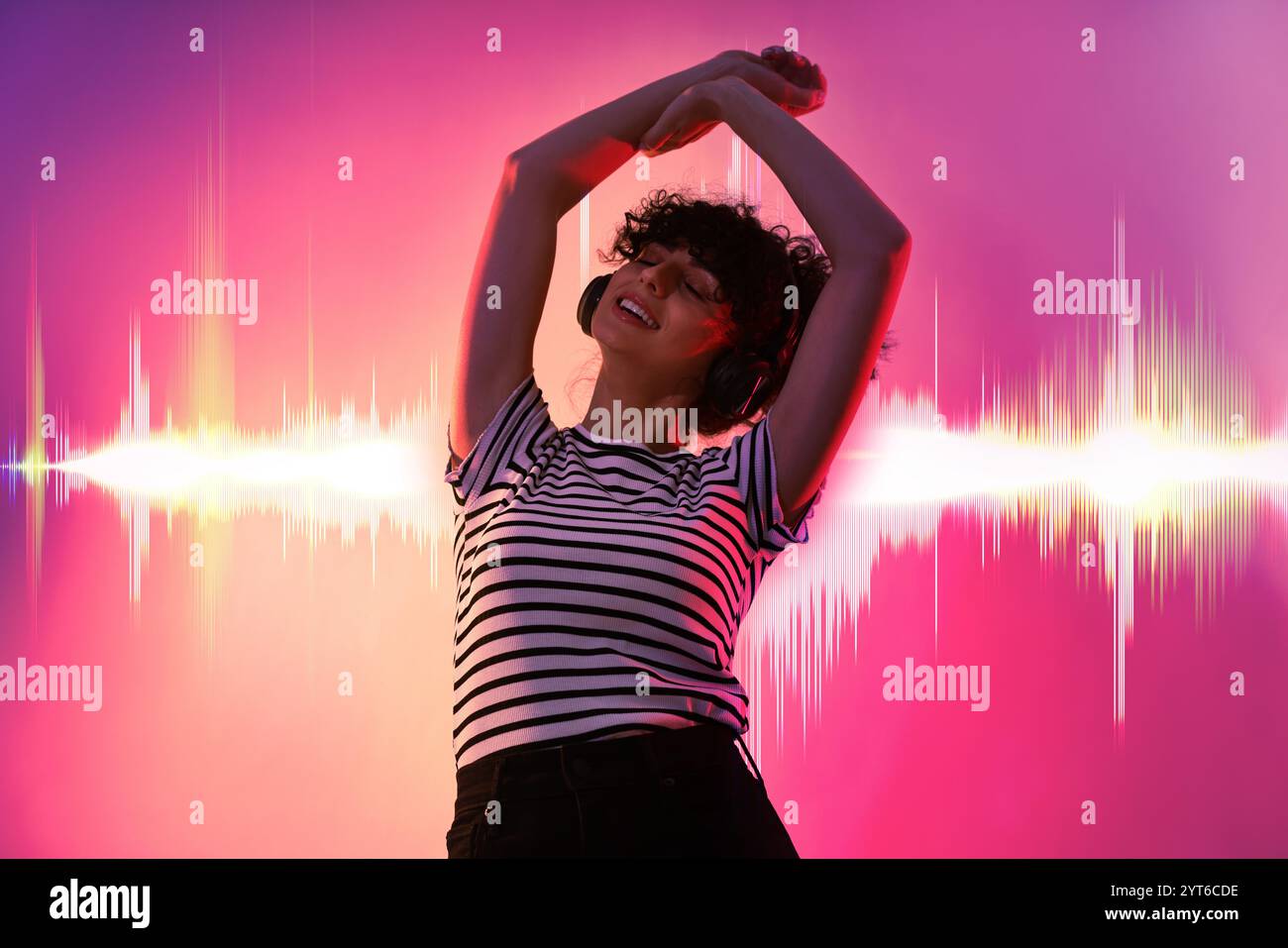 Young woman with headphones listening to music and dancing on color ...