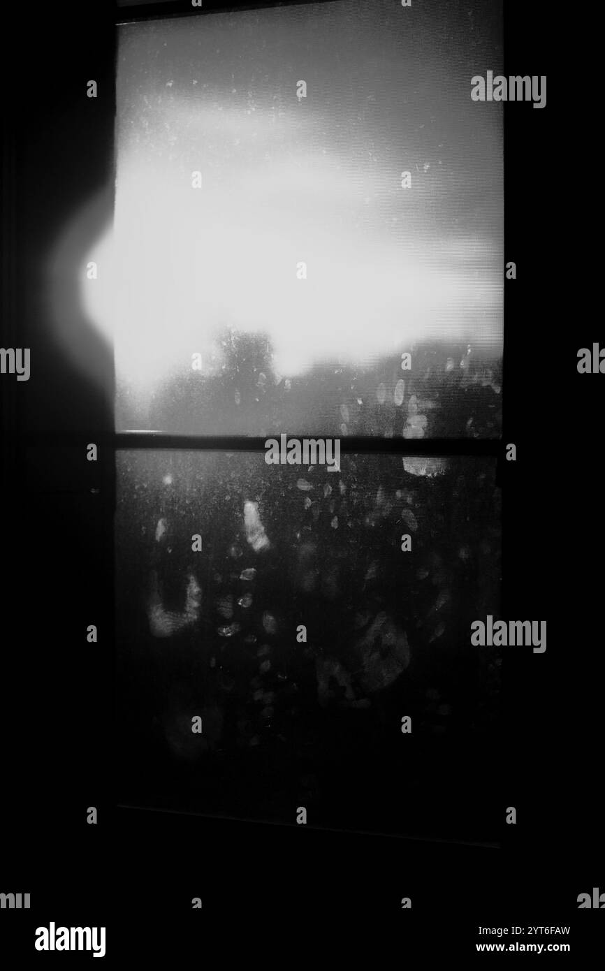 A black-and-white photograph of a window, with human palm prints on the ...