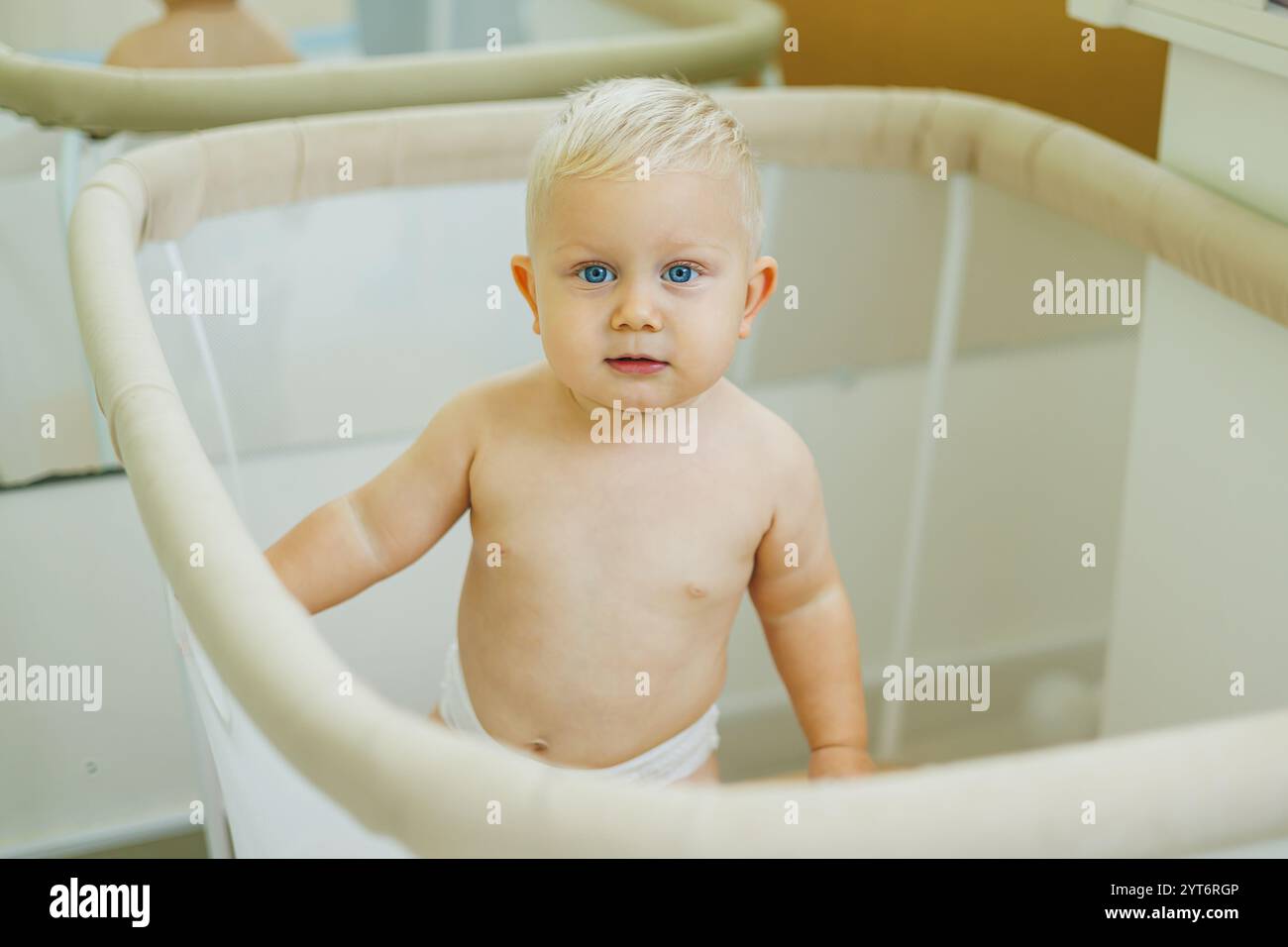 A little boy in a diaper sits in a playpen. A playpen for children ...